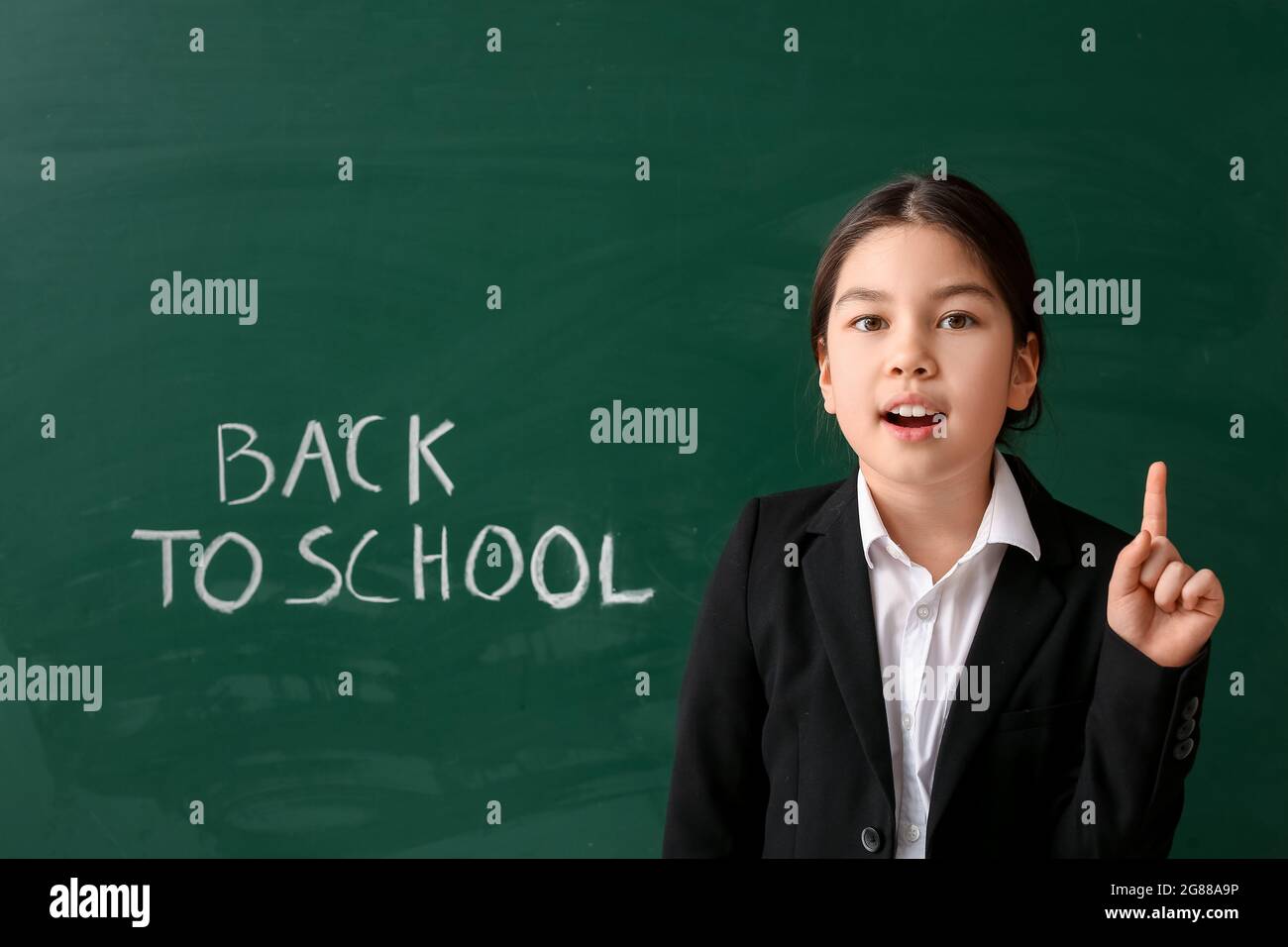 Cute Asian schoolgirl with raised index finger near blackboard in ...