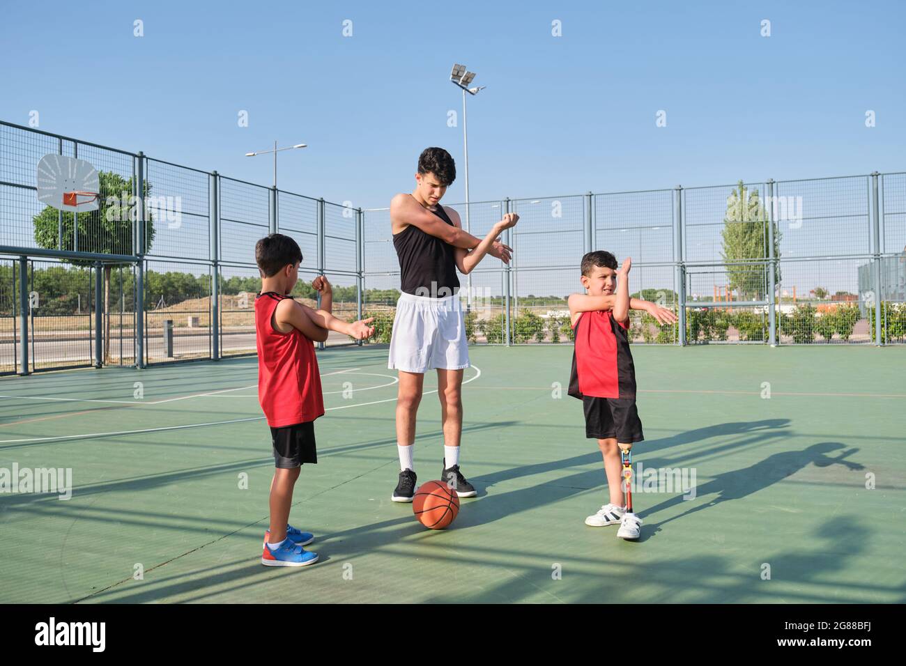 Basketball coach doing arm stretching exercises with two children, one ...