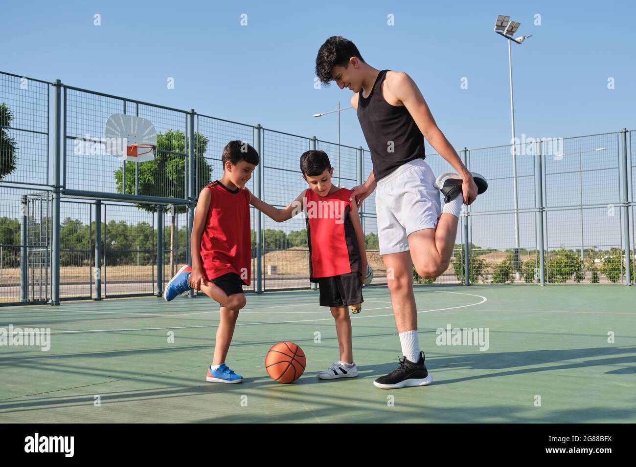 Basketball coach doing leg stretching exercises with two children, one ...
