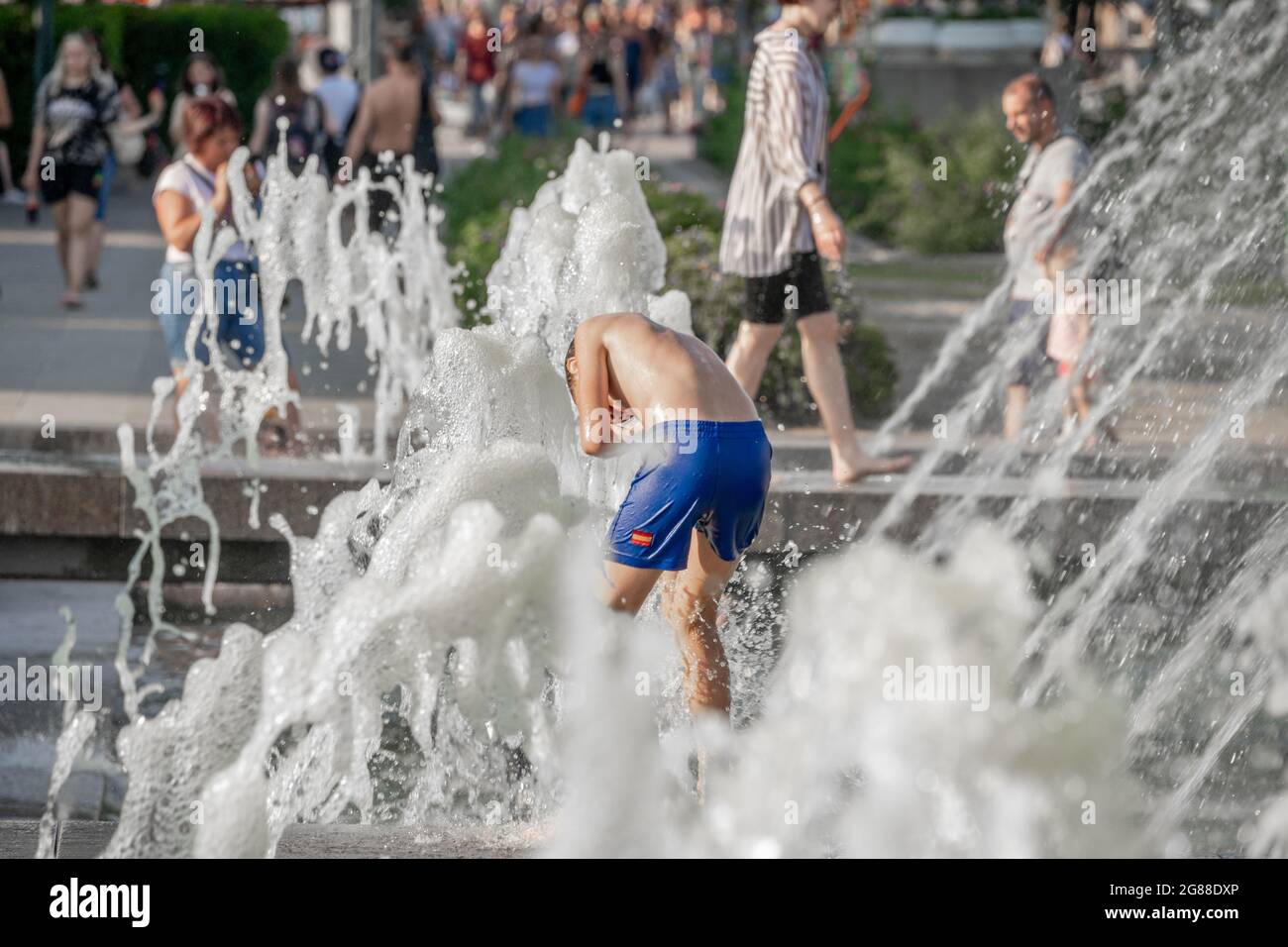 Boy wasning himself in jets of frothing water fountain, in Summer ...