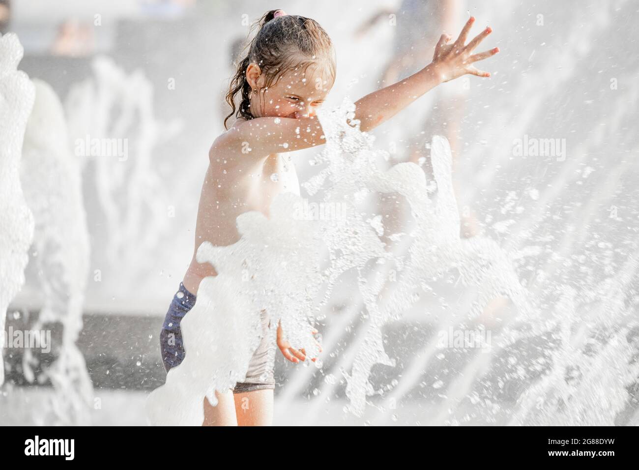 Girl playing in jets of water fountain, seen through sprays and ...