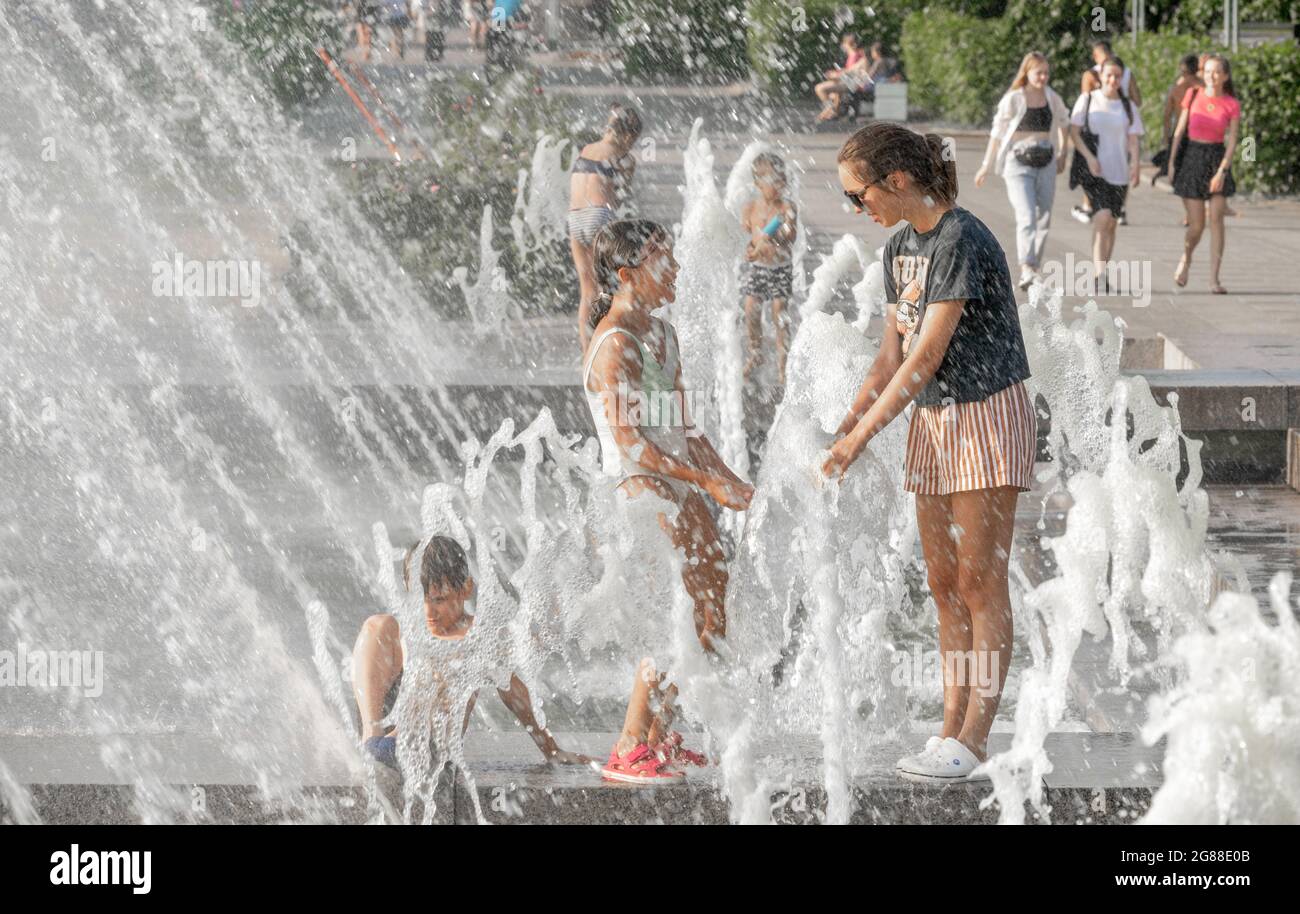 Woman and girl cooling off in jets of water fountain, seen through ...