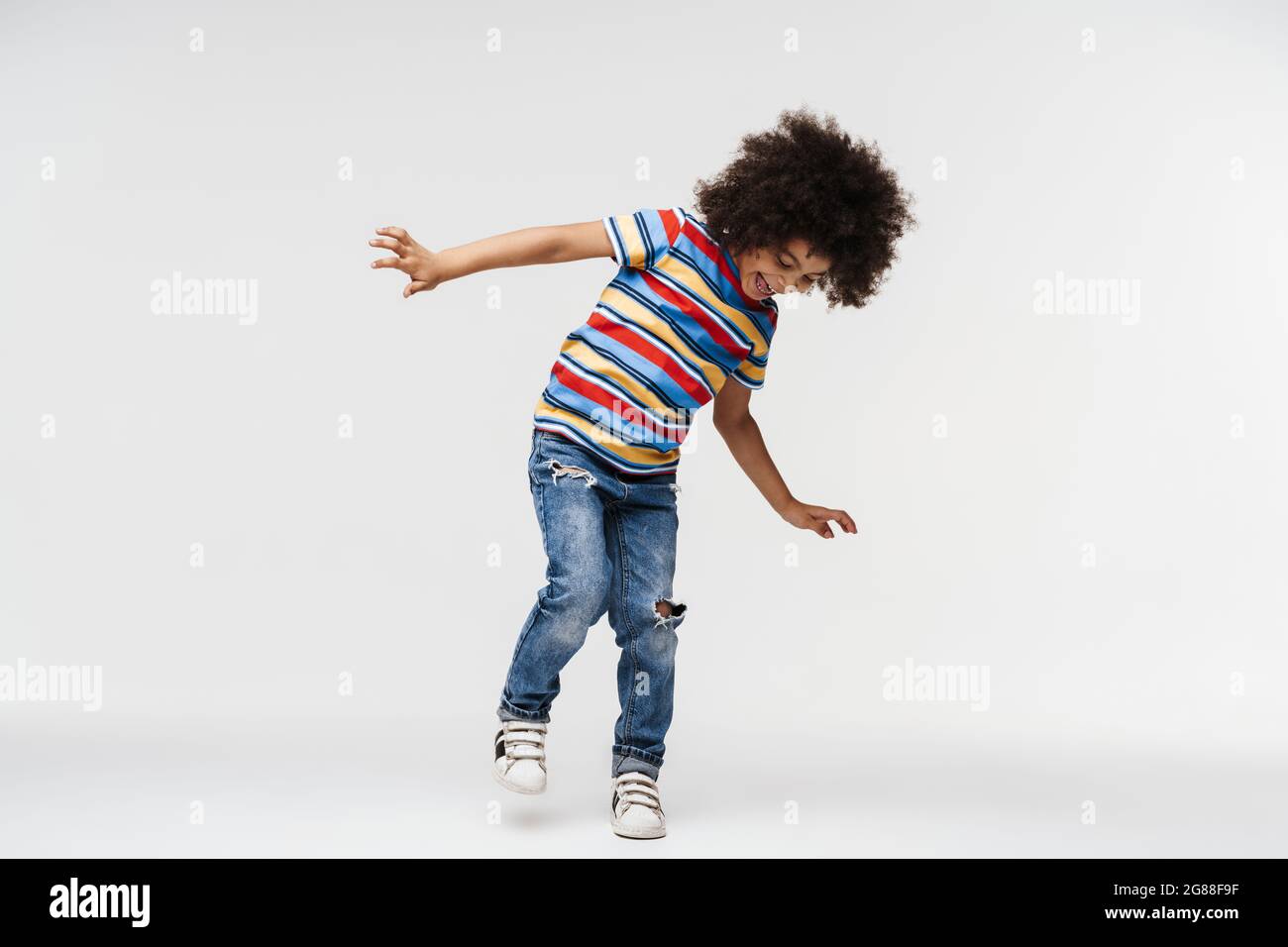 Happy preschooler african boy standing on one leg over white wall ...
