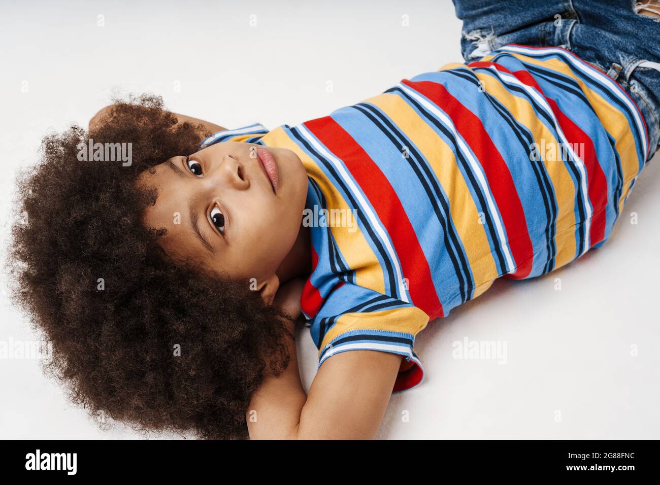 Little african boy in everyday clothes over wall background, laying on ...