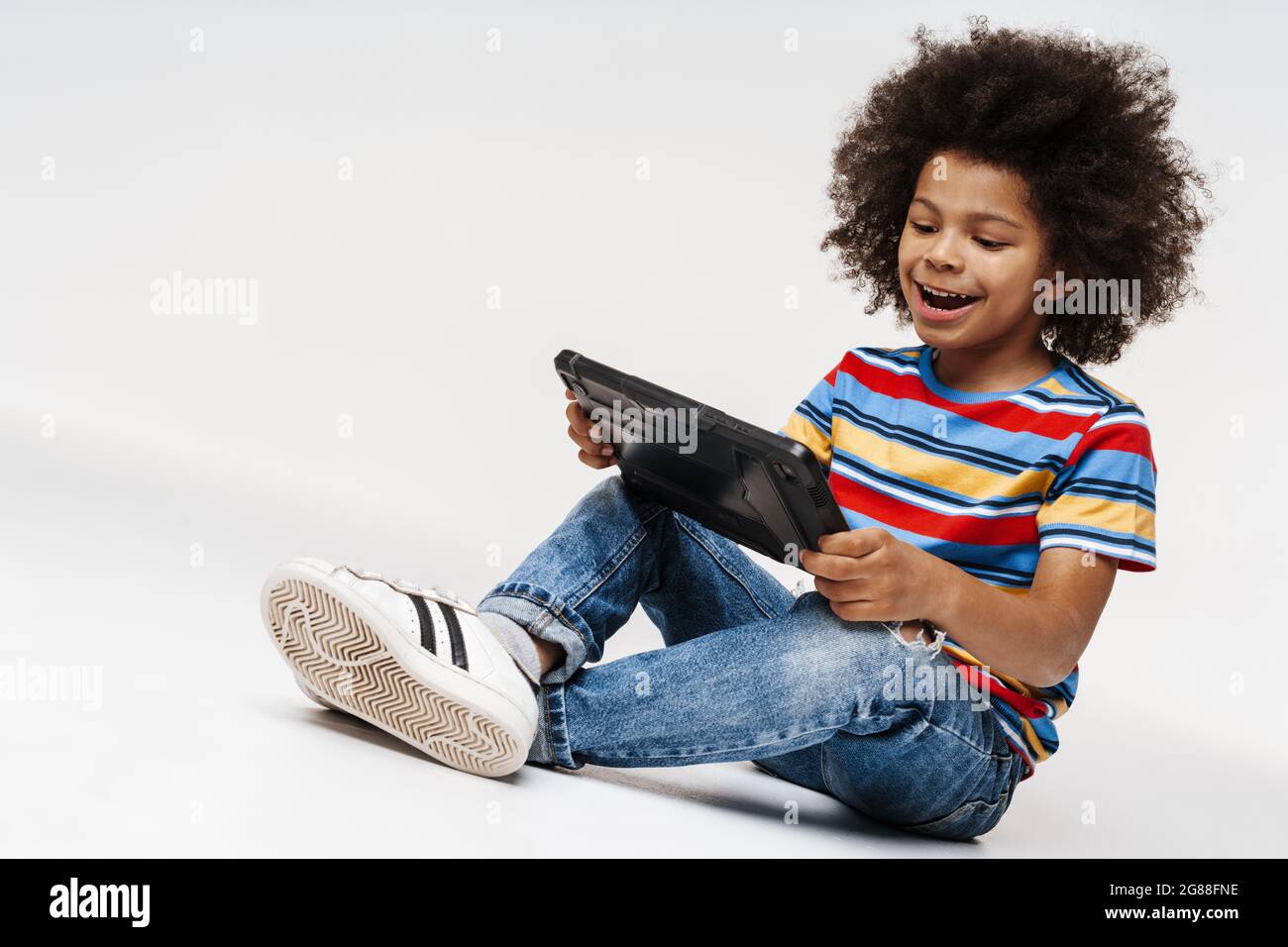 Close up of a little african kid holding tablet over red wall ...