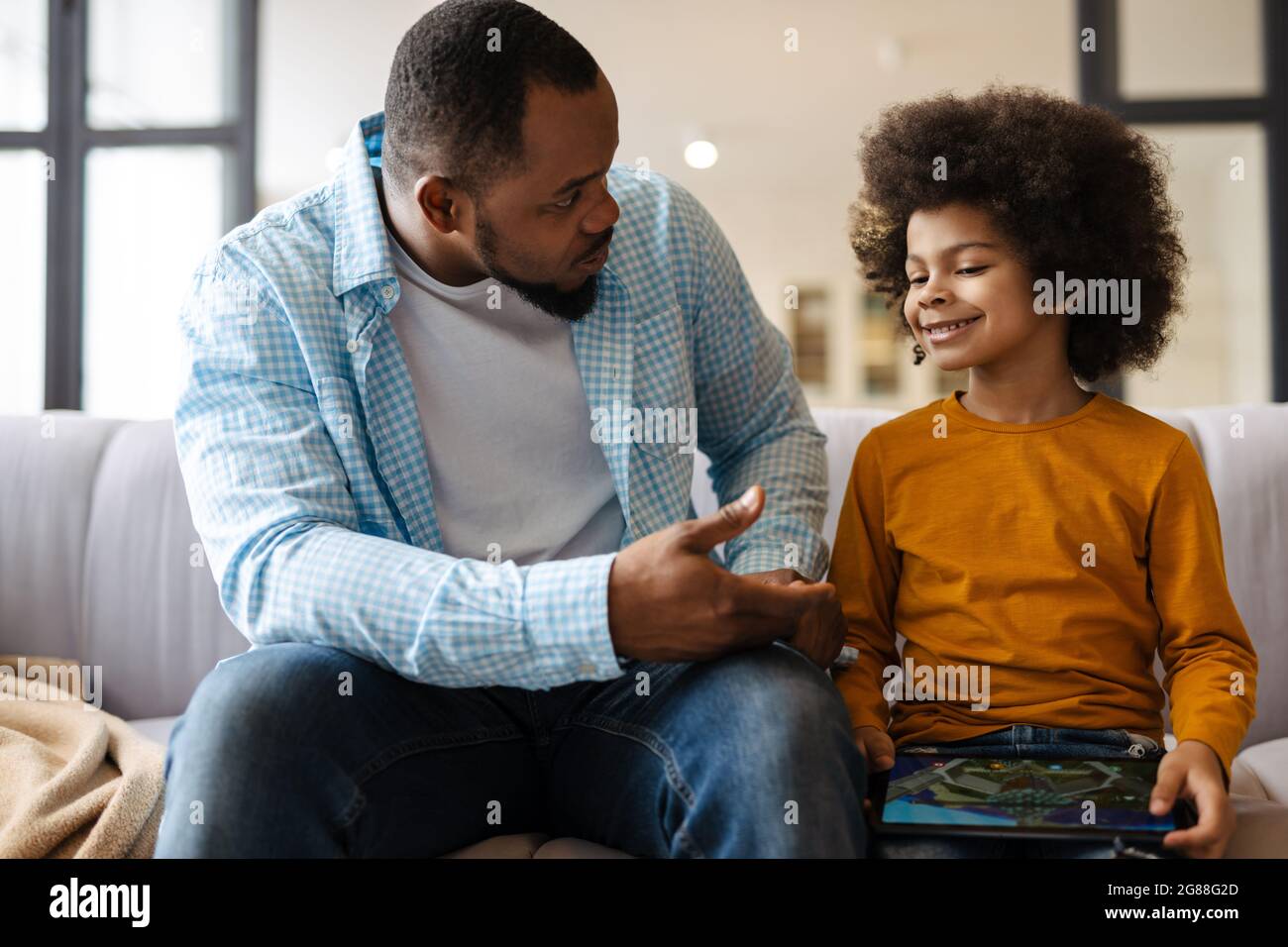 Black father and son talking and using tablet computer while sitting on ...