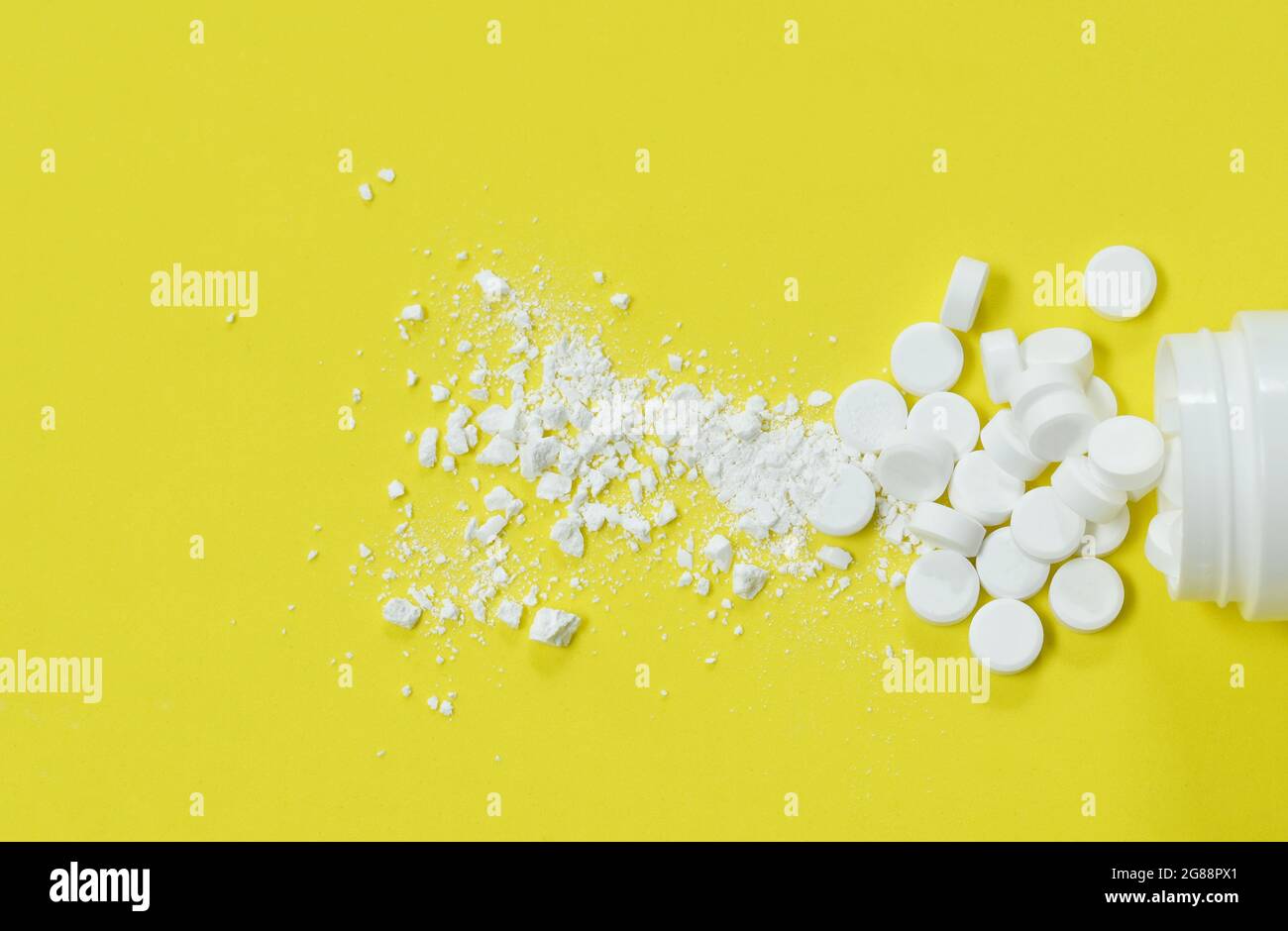 white tablet medicine mashed and pouring from bottle on yellow ...