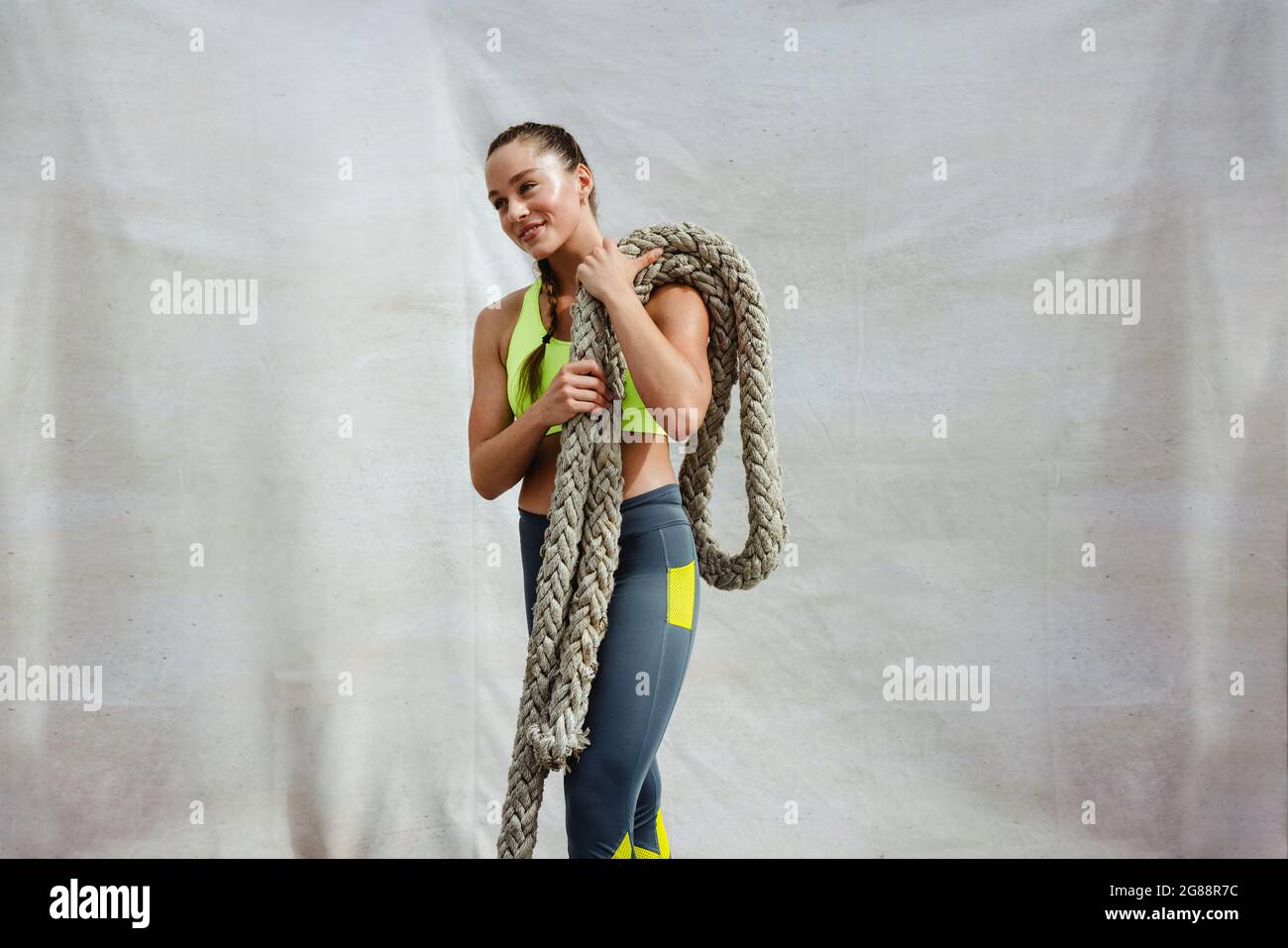 fitness woman in exercise outfit lifting battle rope and standing on ...