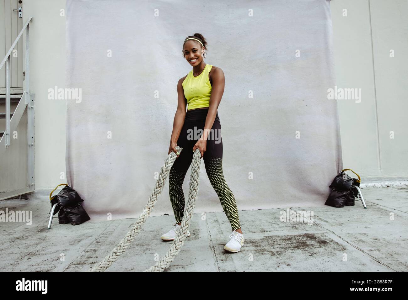 African woman in fitness wear cross training with battle rope. Female ...