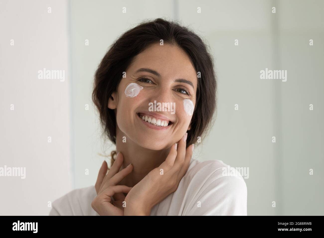 Happy hispanic woman pampering face skin with natural cosmetic creme ...