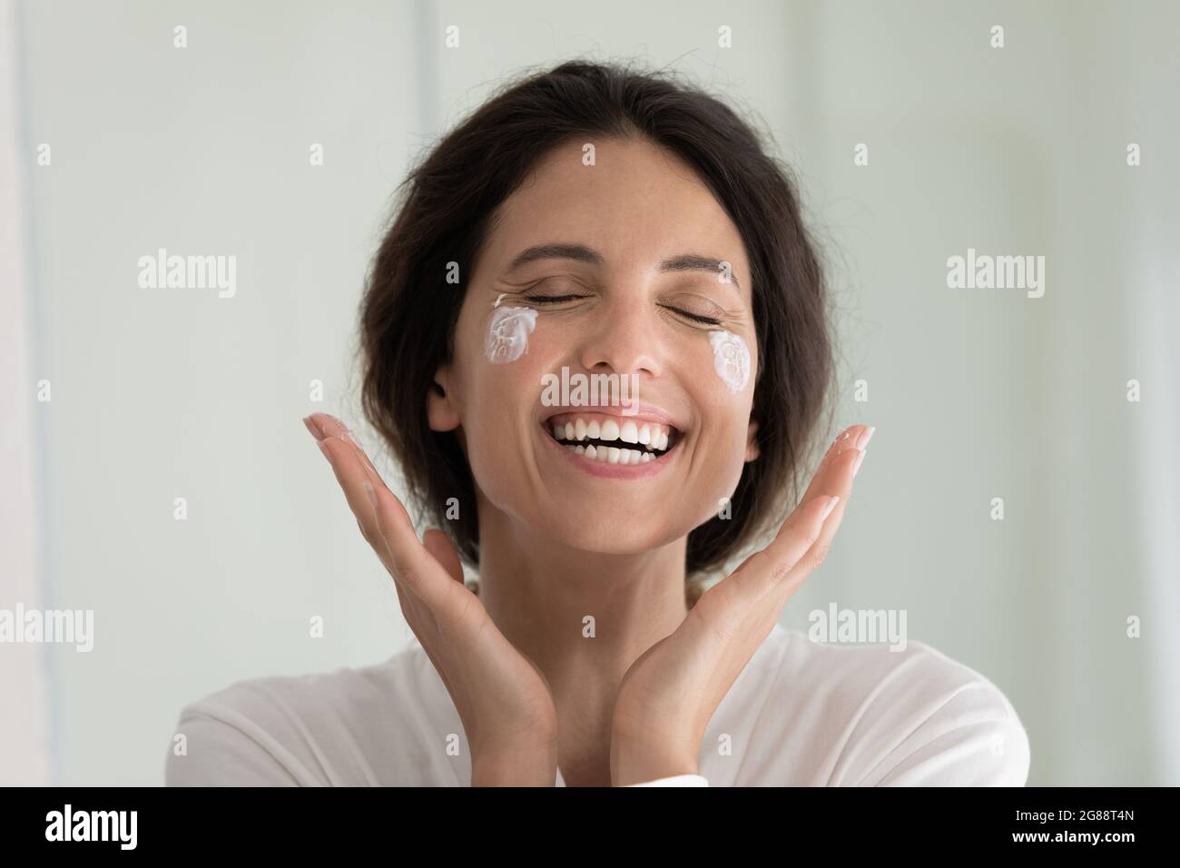 Overjoyed millennial latina woman feel pleasure applying cream on face ...
