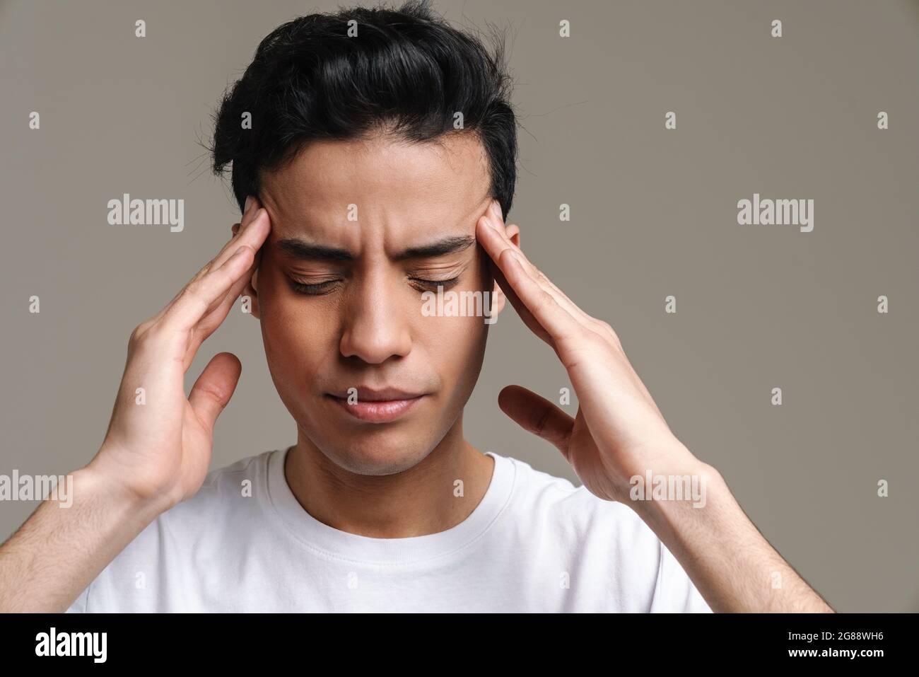 Brunette hispanic man with headache frowning and rubbing his temples ...