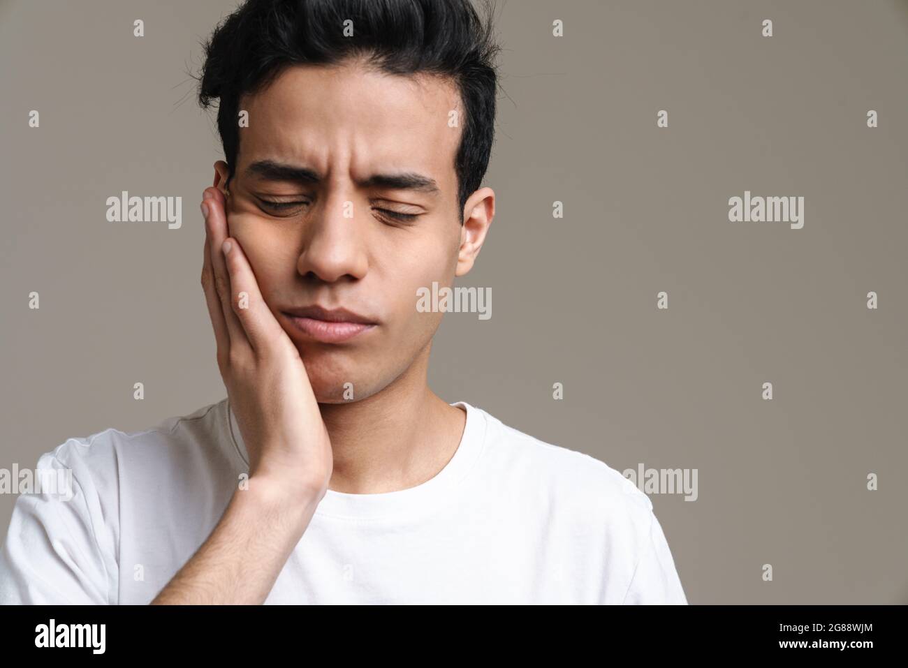 Brunette hispanic man with toothache frowning and rubbing his cheek ...