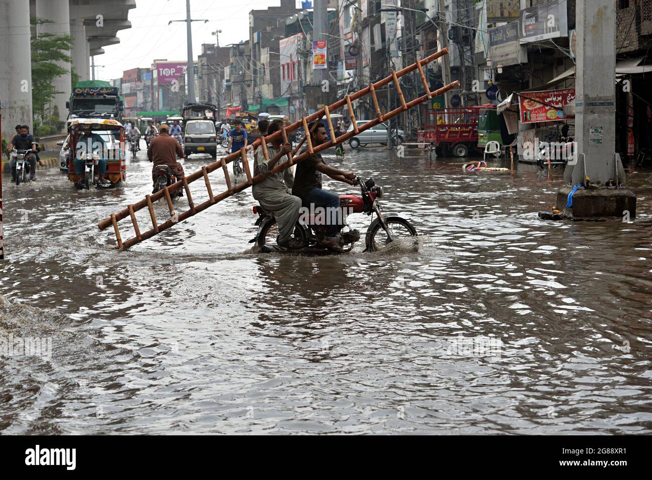 Lahore, Pakistan. 18th July, 2021. Pakistani commuters wade through a flooded street and Baghban ...