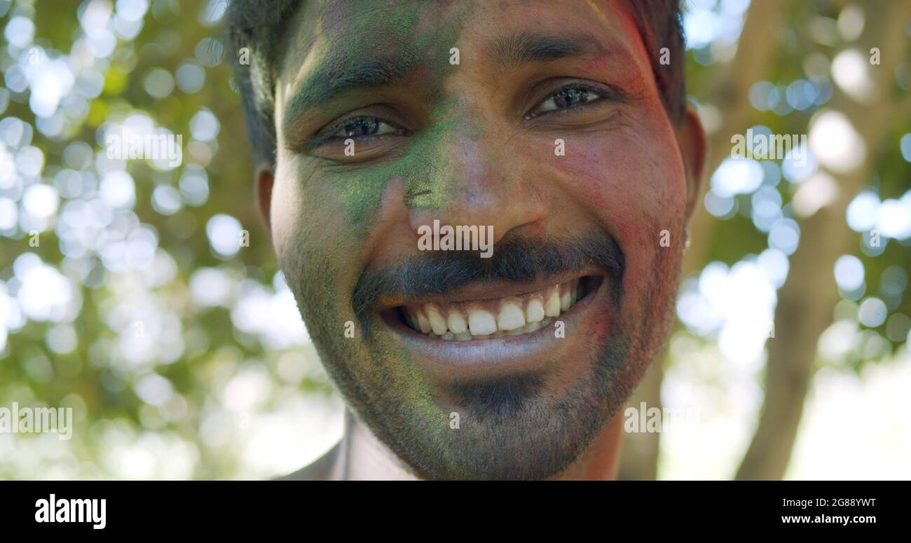 A smiling Indian guy with a painted face is having fun at the Holi ...