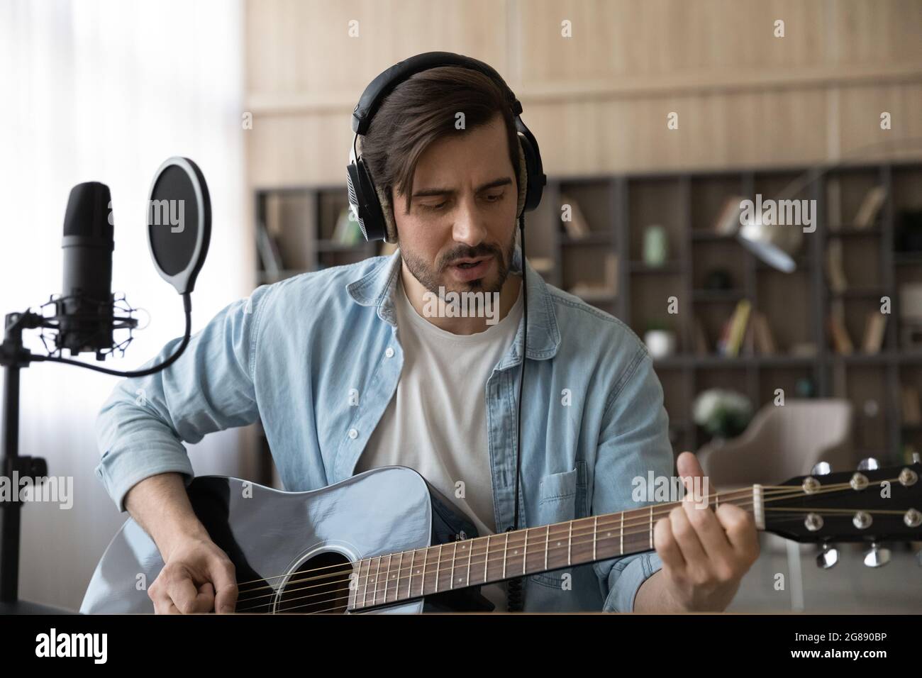 Happy millennial male musician playing guitar, recording own music ...