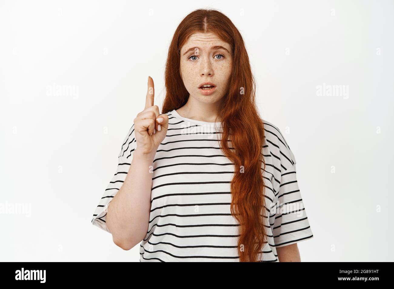 Surprised redhead girl with natural long hair, pointing finger up with ...