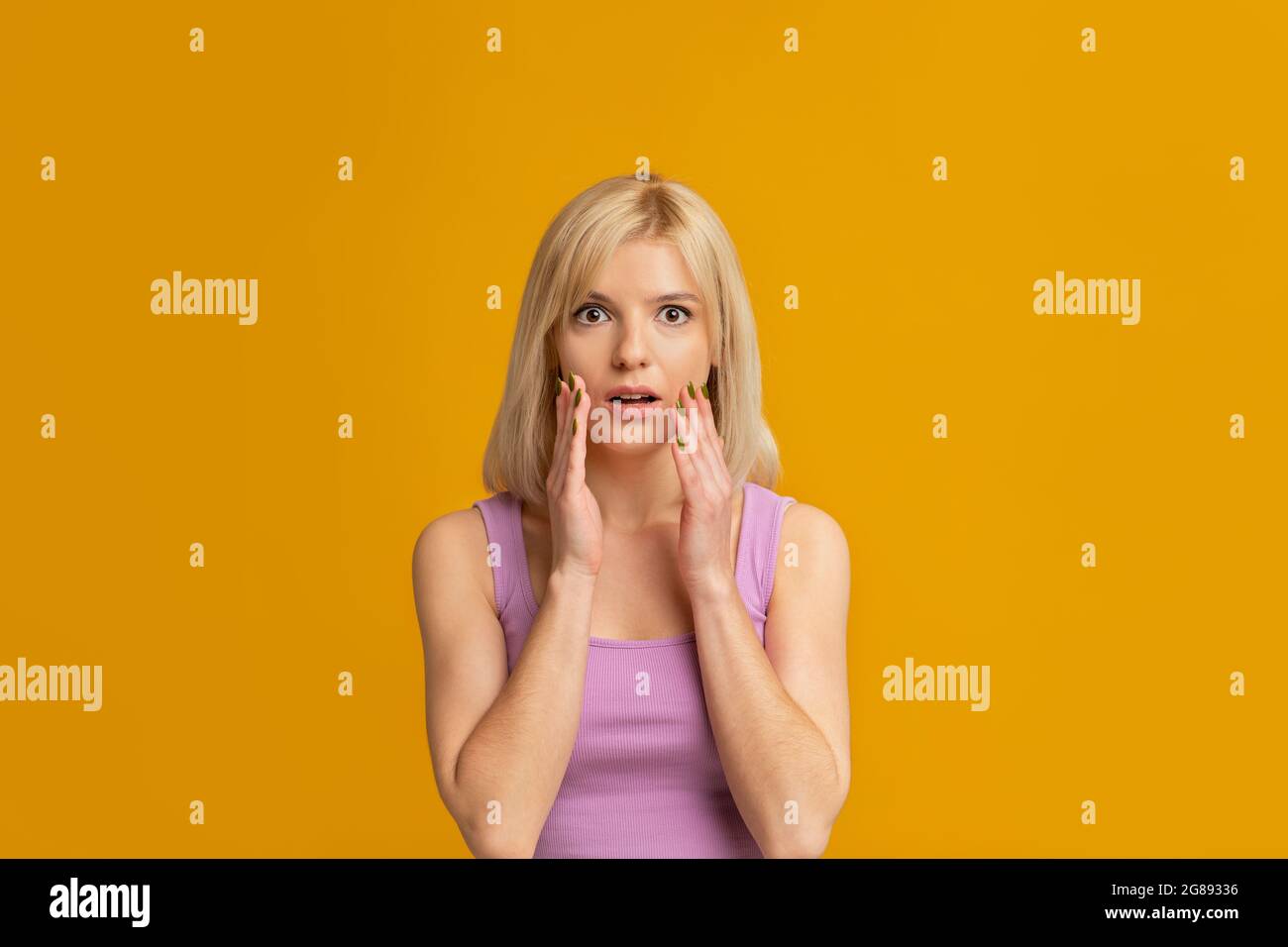 Oh no. Shocked young lady looking at camera and covering mouth with ...