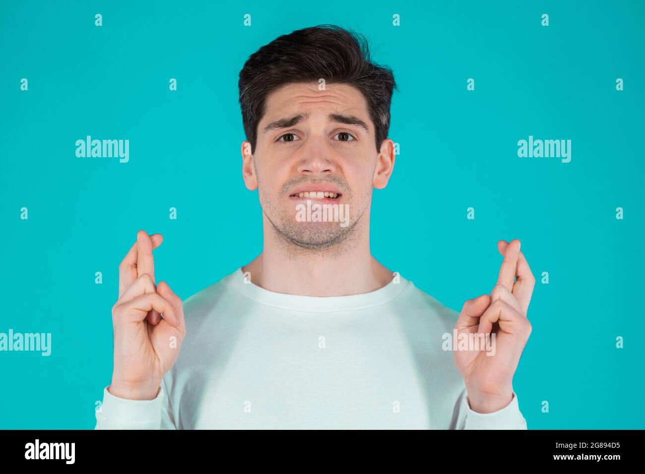 Young man praying over blue background. Guy in white wear begging ...