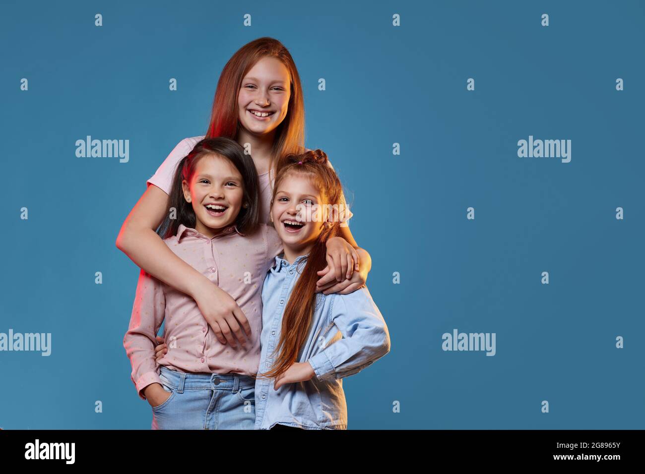 three kids girls standing together on blue background Stock Photo - Alamy