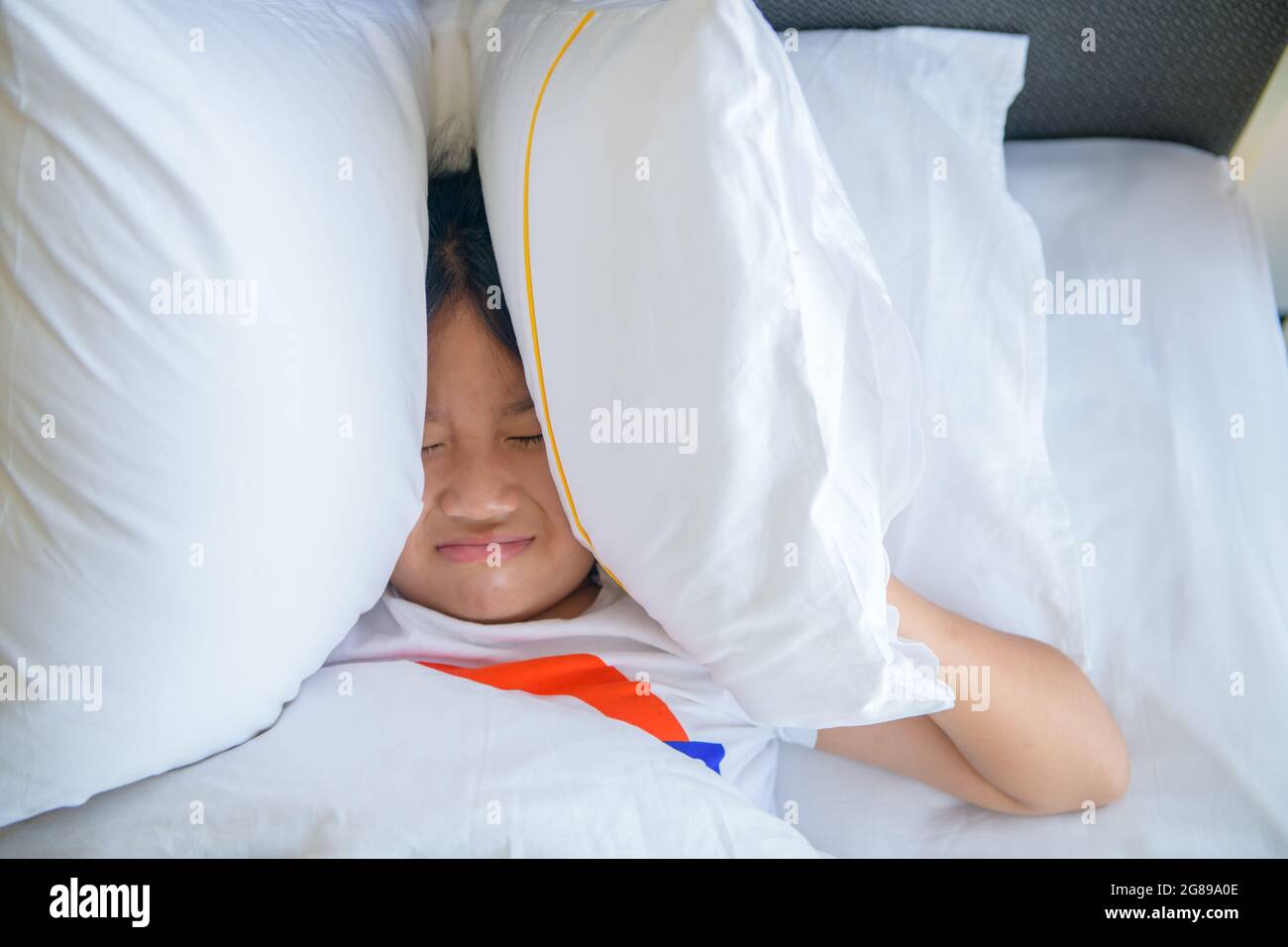 Little girl lying in bed covering head with pillow because too loud ...
