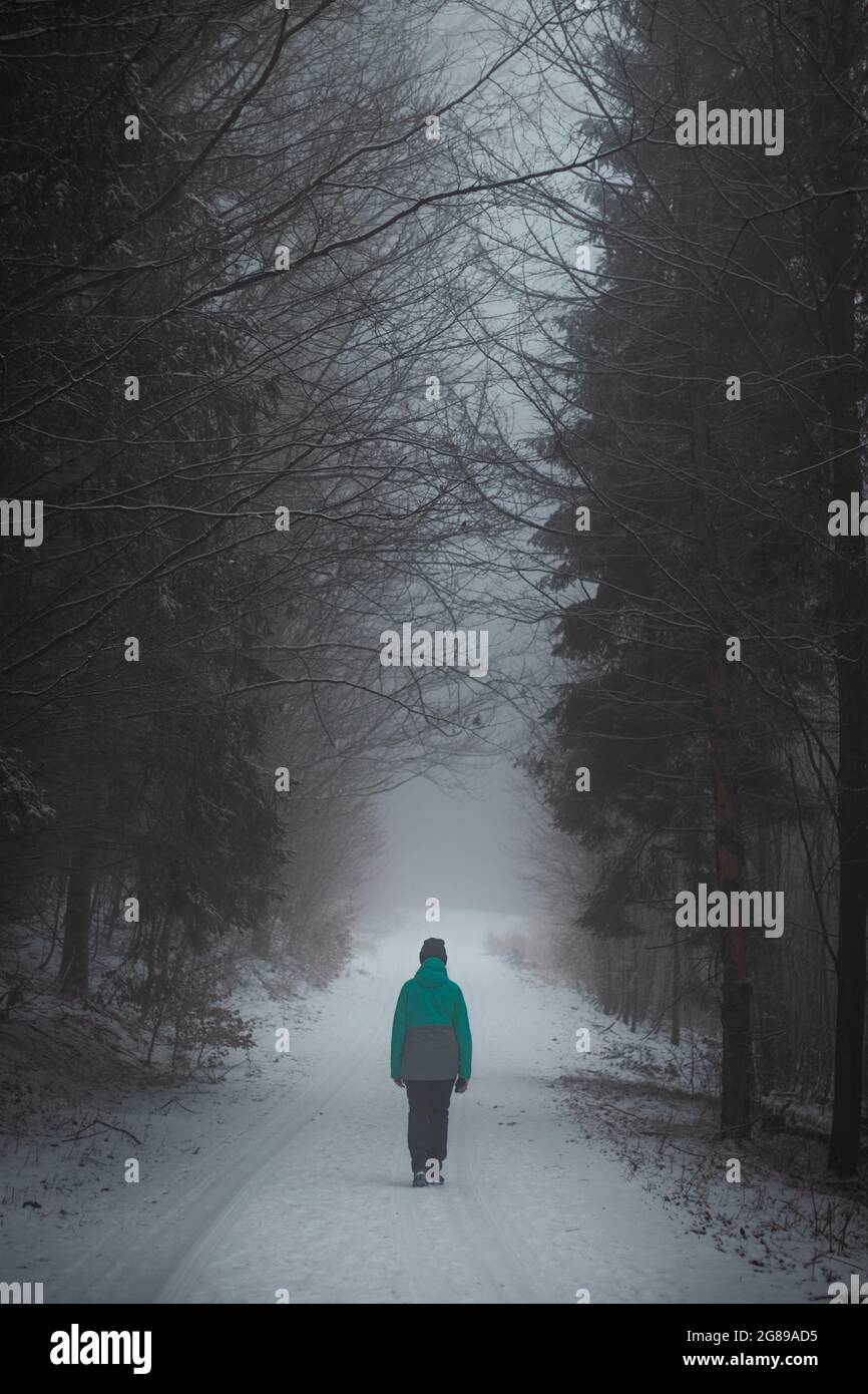 young girl in a green winter jacket walks in the ugly, foggy and cold ...