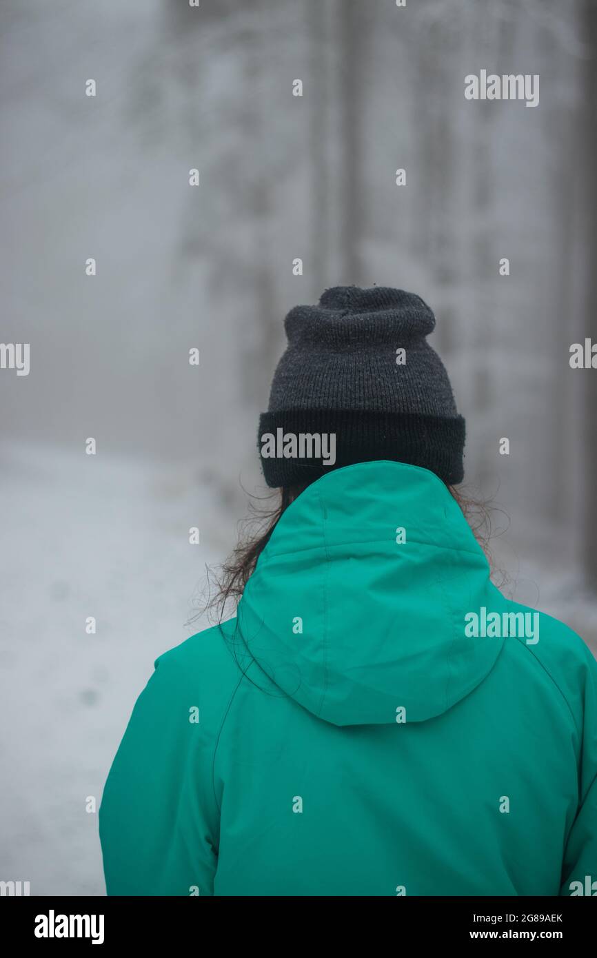young girl in a green winter jacket walks in the ugly, foggy and cold ...