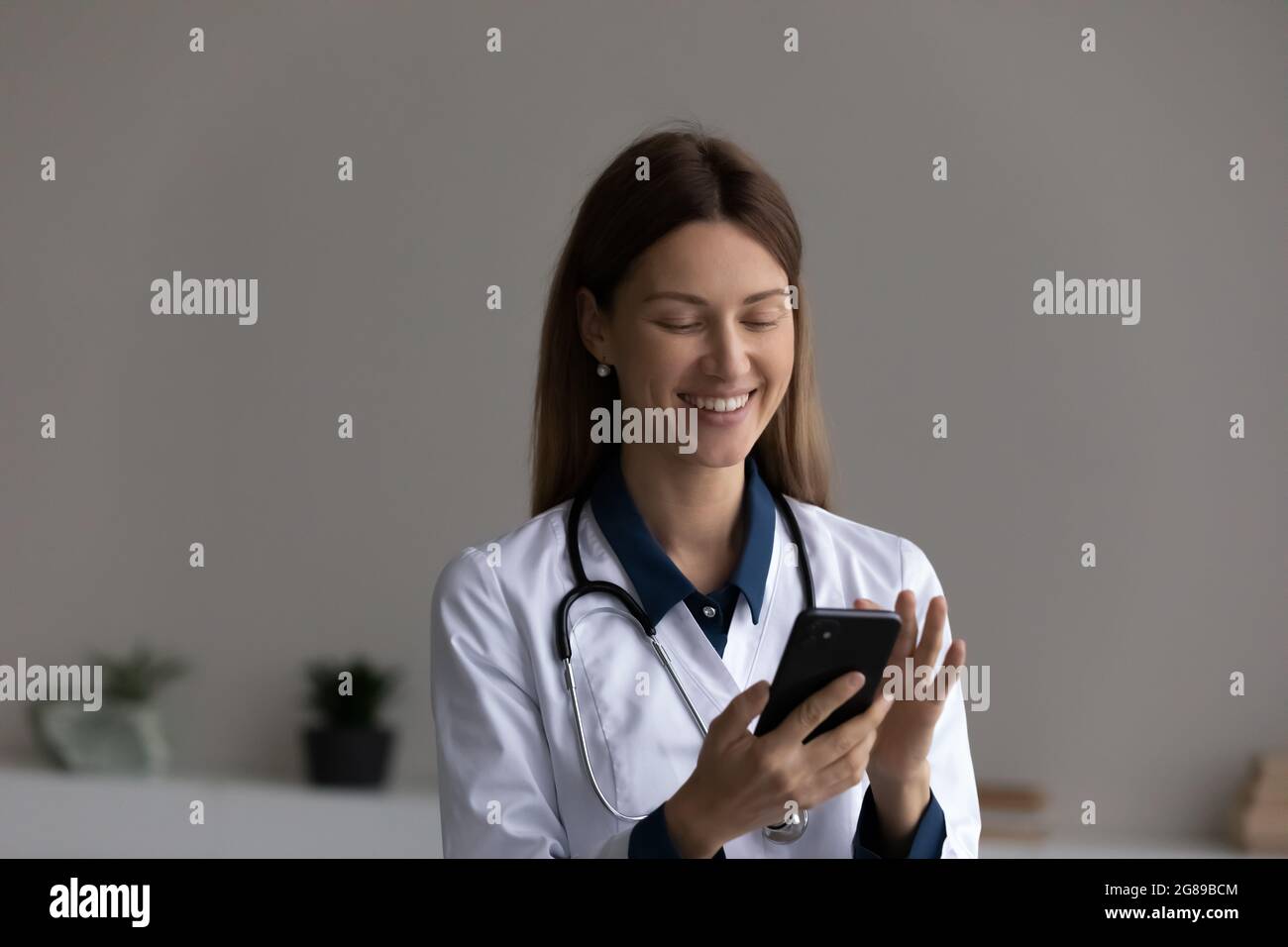 Happy female doctor using app on smartphone for making appointment ...