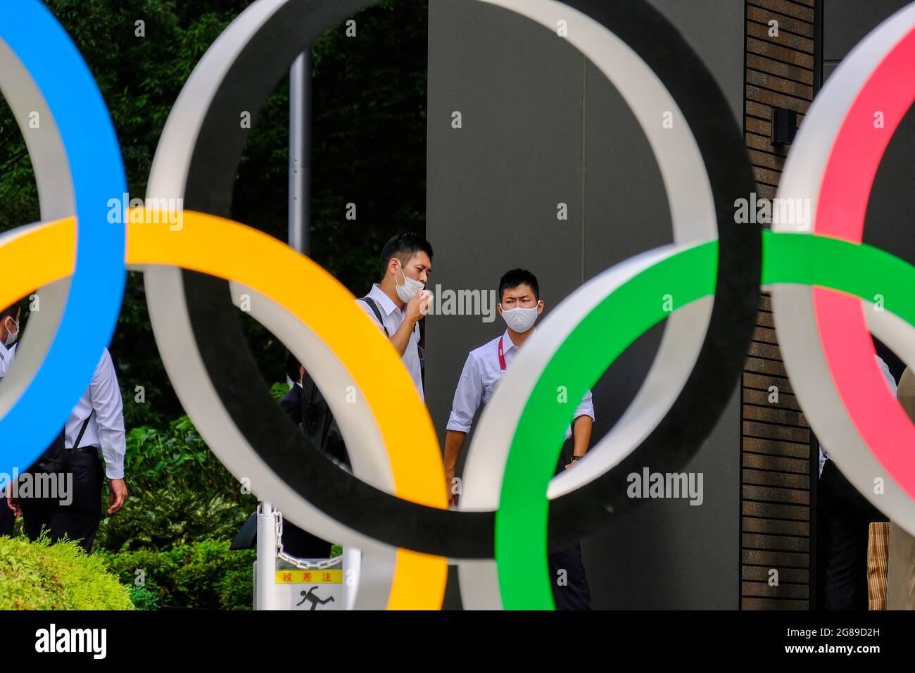 People wearing face masks walk past the Olympic Rings near the National ...