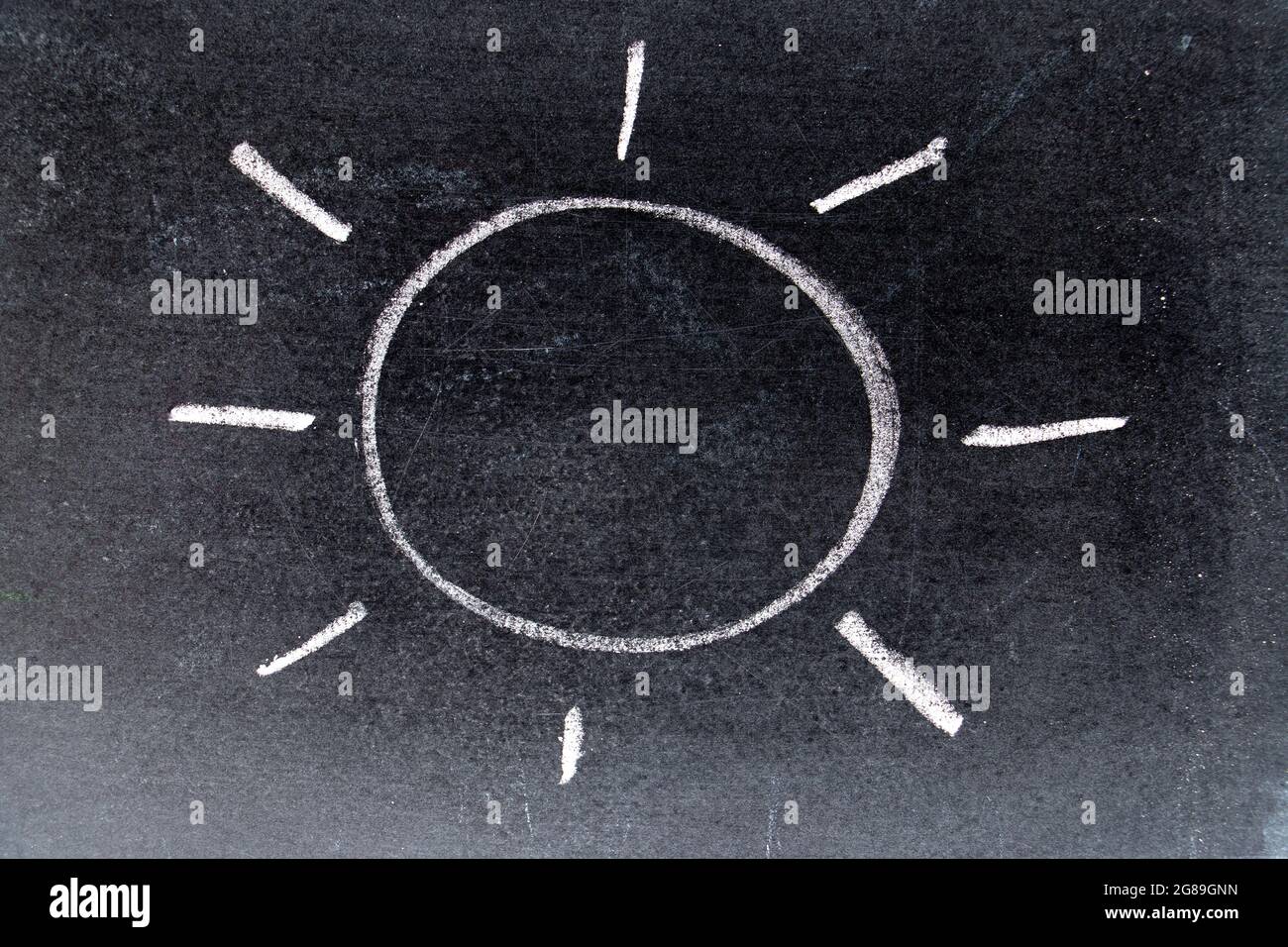 White chalk hand drawing in sun with ray shape on black board ...