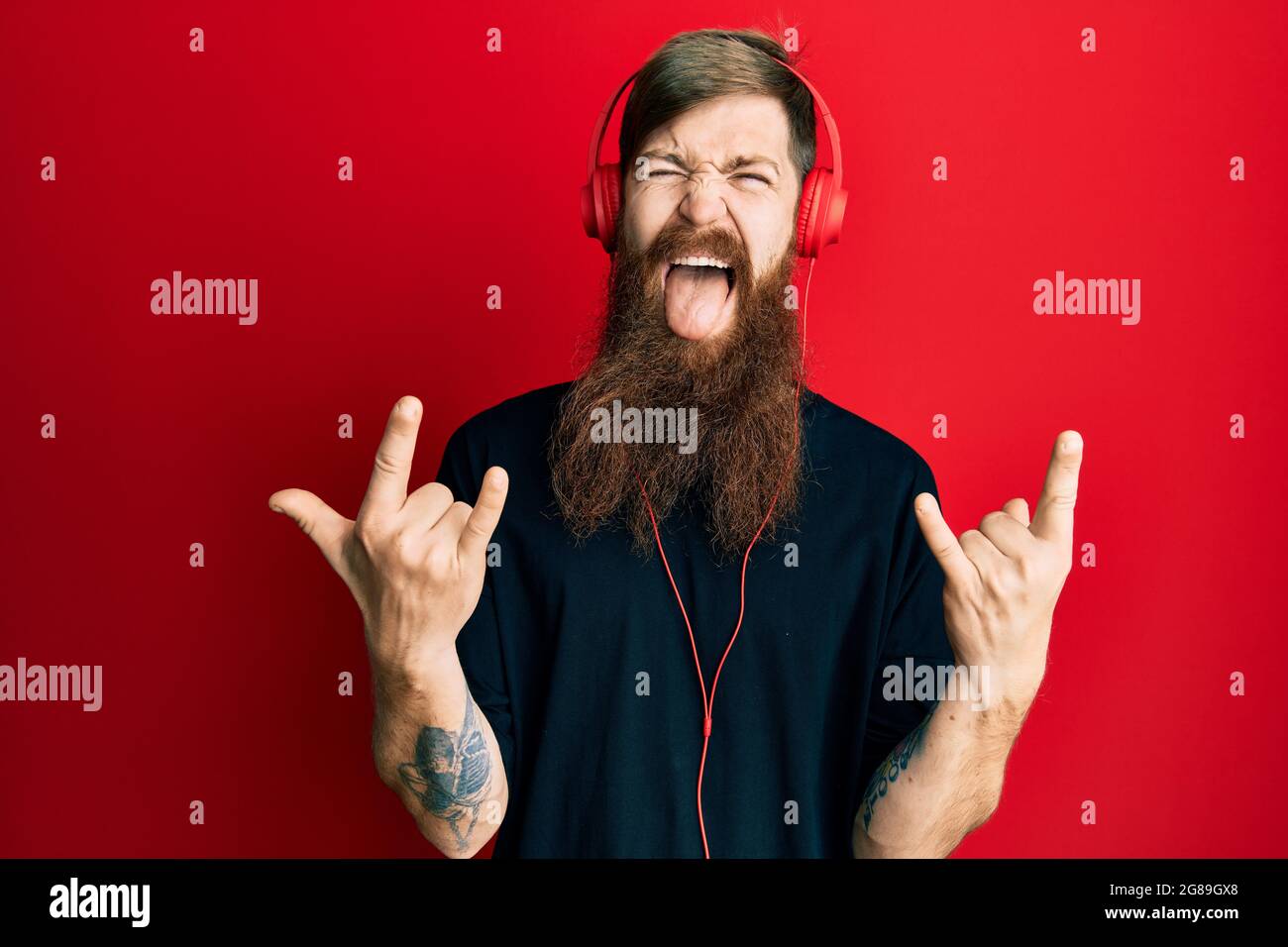 Redhead man with long beard listening to music using headphones ...