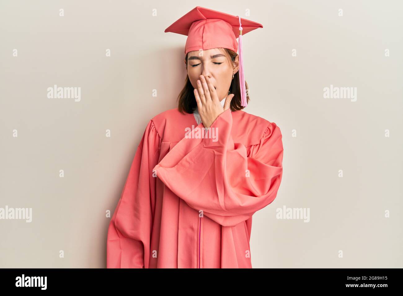 Young caucasian woman wearing graduation cap and ceremony robe bored ...