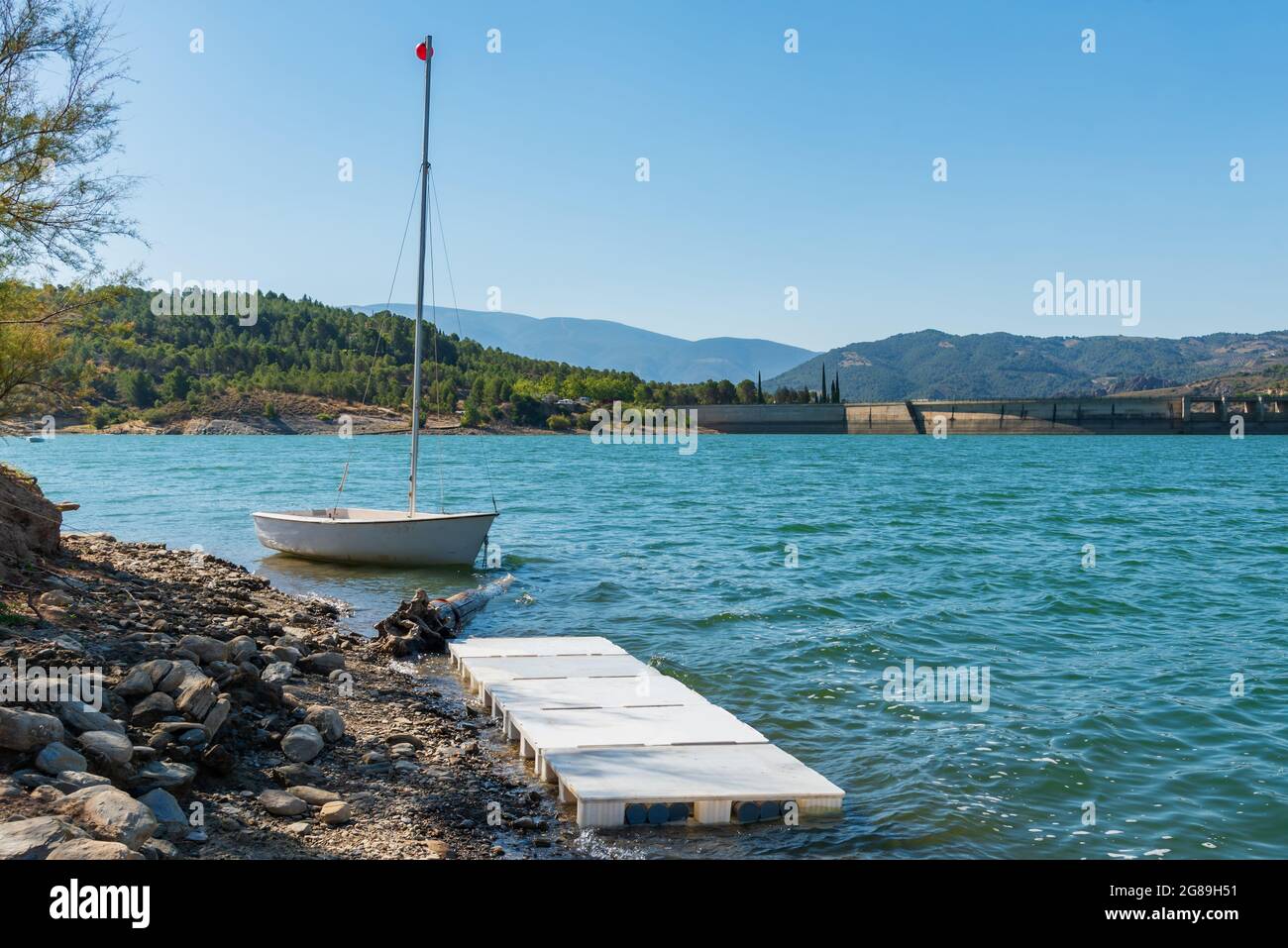Sailing boat moored on the shore to a wooden log next to a small ...
