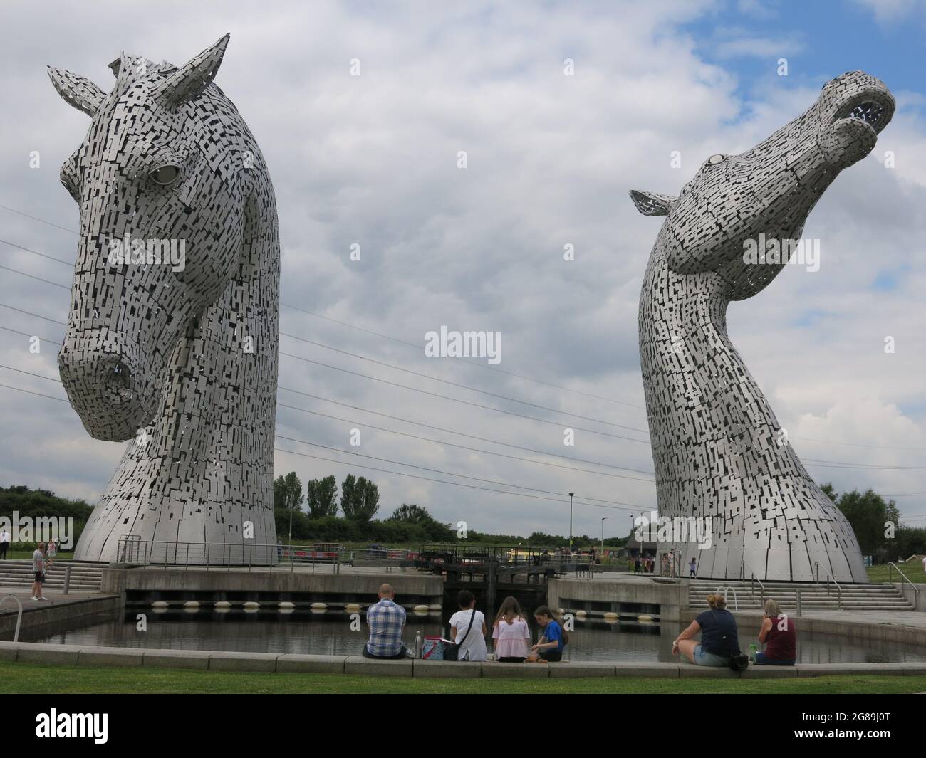 Visitors sitting on a wall to gaze up & admire The Kelpies, two 30m ...