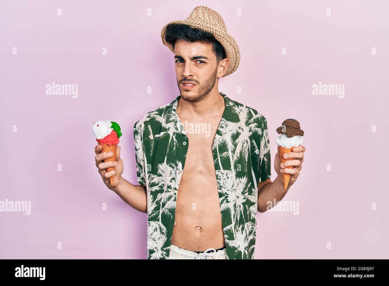 Young hispanic man wearing summer style holding ice cream clueless and ...