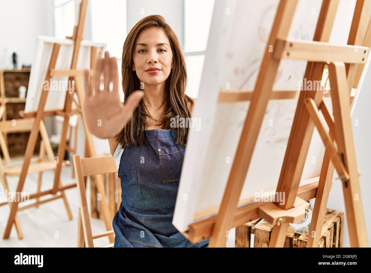 Young latin artist woman painting at art studio with open hand doing ...