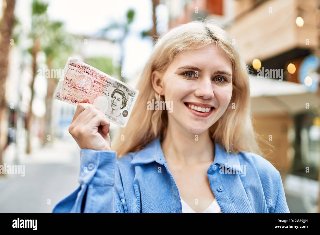 Young blonde woman holding english banknotes pounds, showing money ...