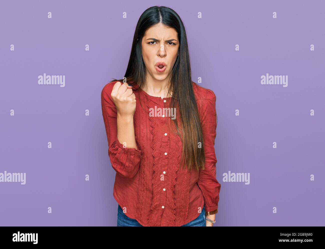 Young hispanic woman wearing casual clothes angry and mad raising fist ...