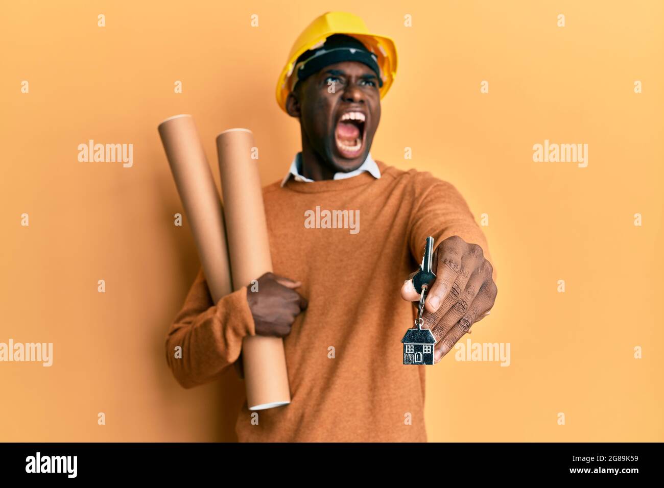 Young african american man wearing safety helmet holding blueprints and ...