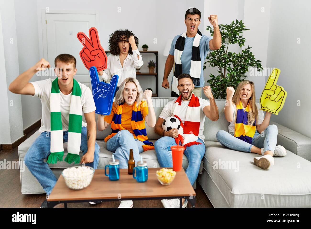 Group of friends supporting football team watching tv al home sitting ...