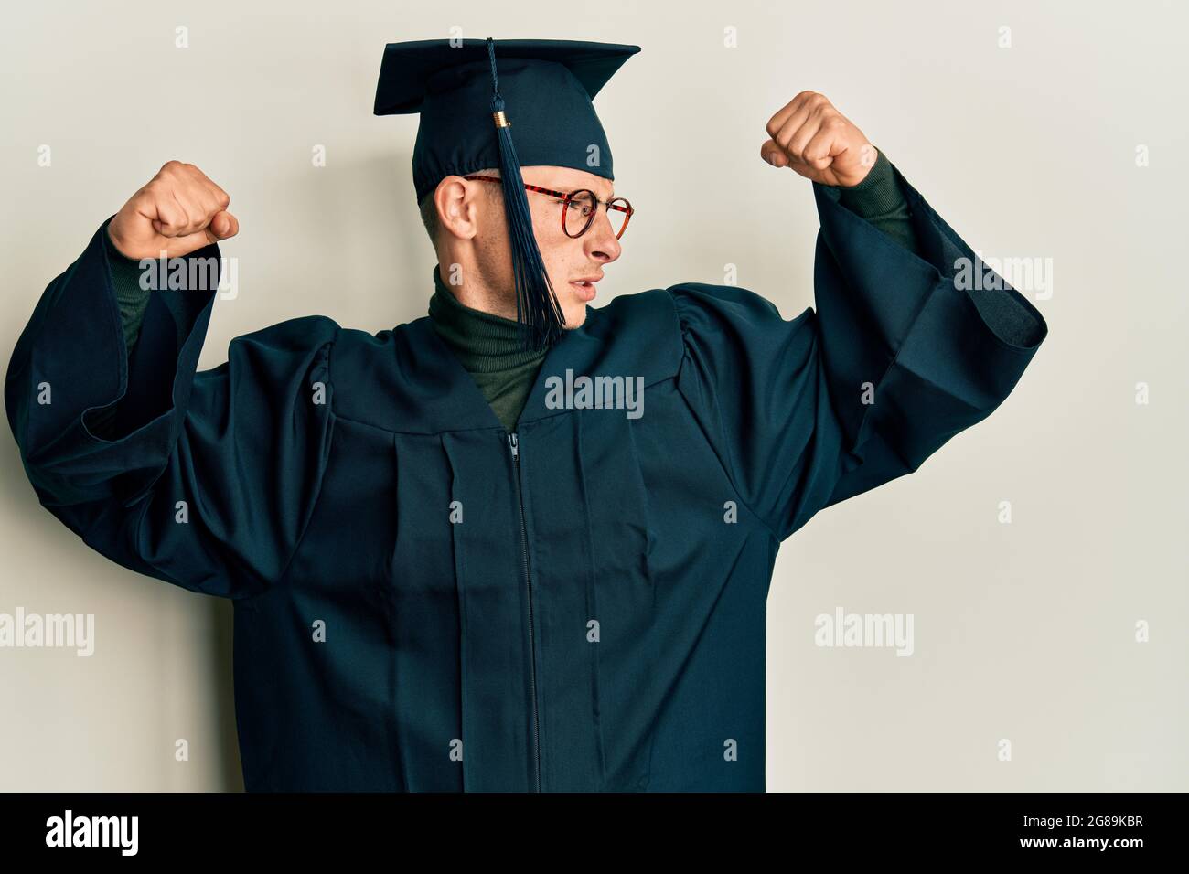 Young caucasian man wearing graduation cap and ceremony robe showing ...