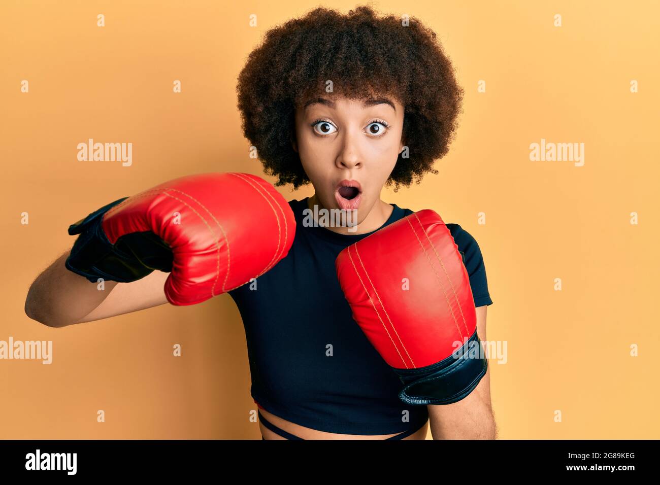 Young hispanic sporty girl using boxing gloves afraid and shocked with ...
