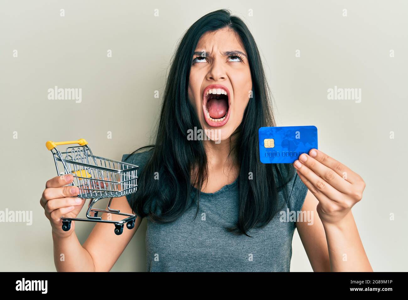 Young hispanic woman holding small supermarket shopping cart and credit ...