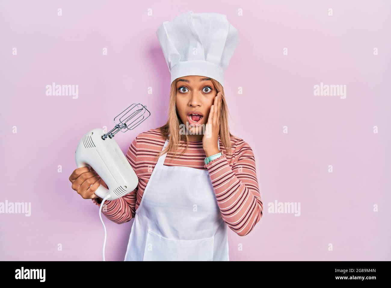 Beautiful hispanic woman holding pastry blender electric mixer afraid ...