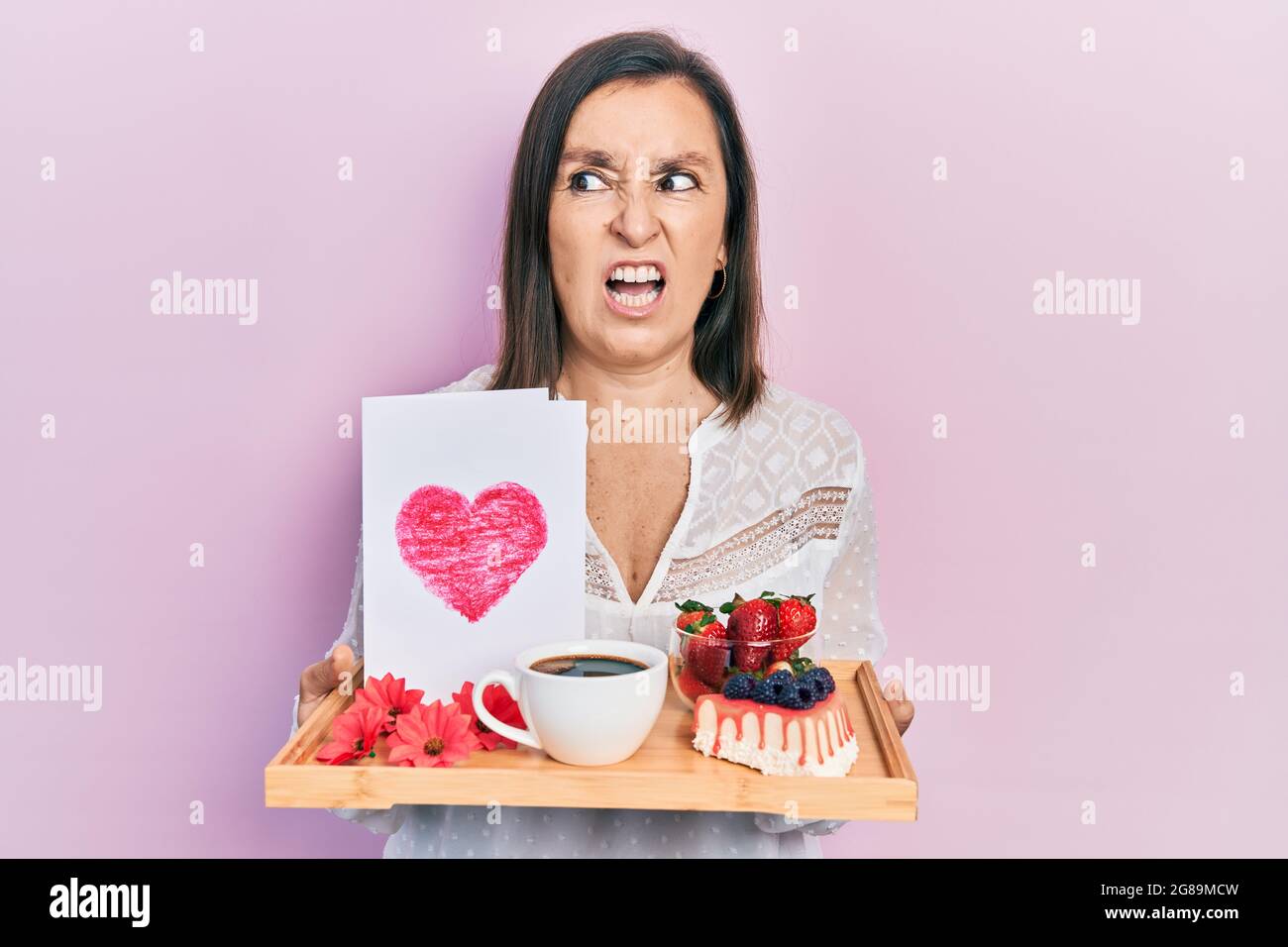 Middle age hispanic woman holding tray with breakfast food and heart ...