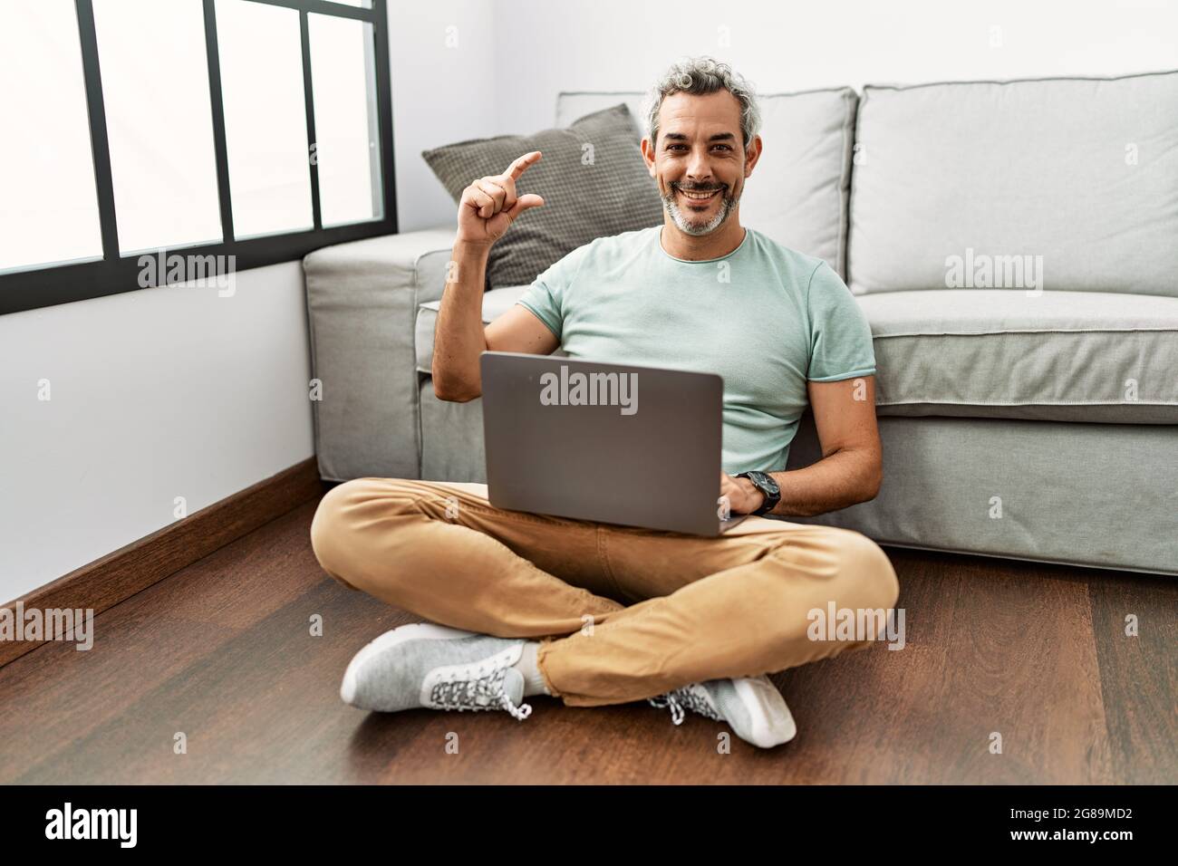Middle age hispanic man using laptop sitting on the floor at the living ...