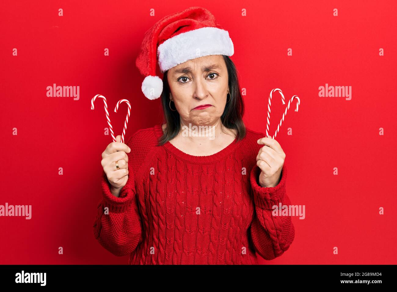 Middle Age Hispanic Woman Wearing Christmas Hat Holding Candy Depressed