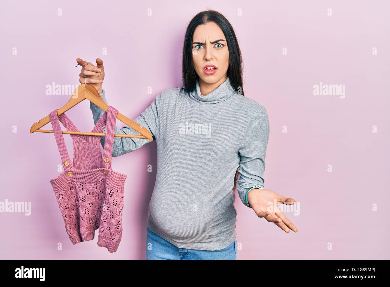 Beautiful woman with blue eyes expecting a baby holding baby clothes ...