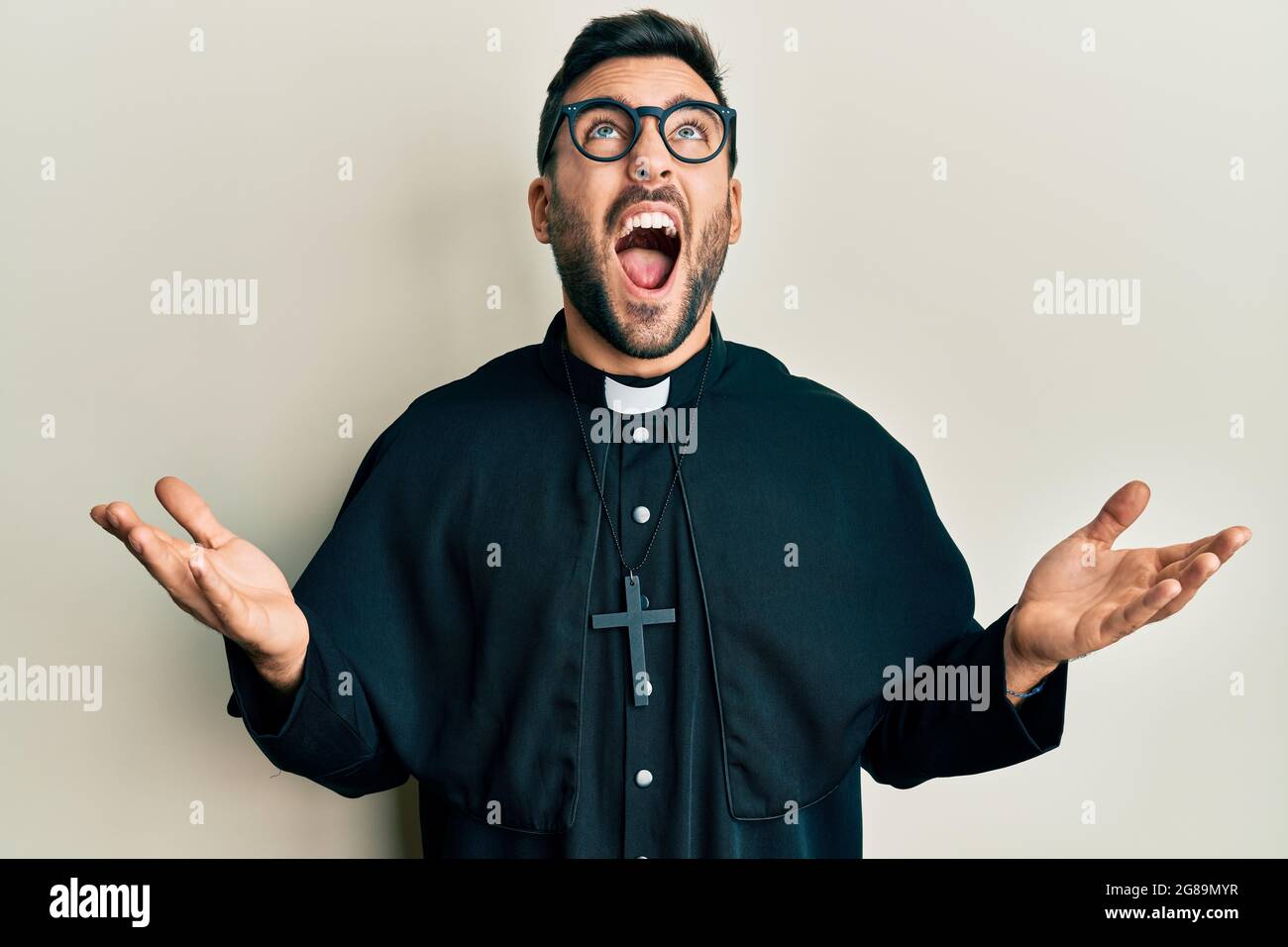 Young hispanic priest man standing over white background angry and mad ...