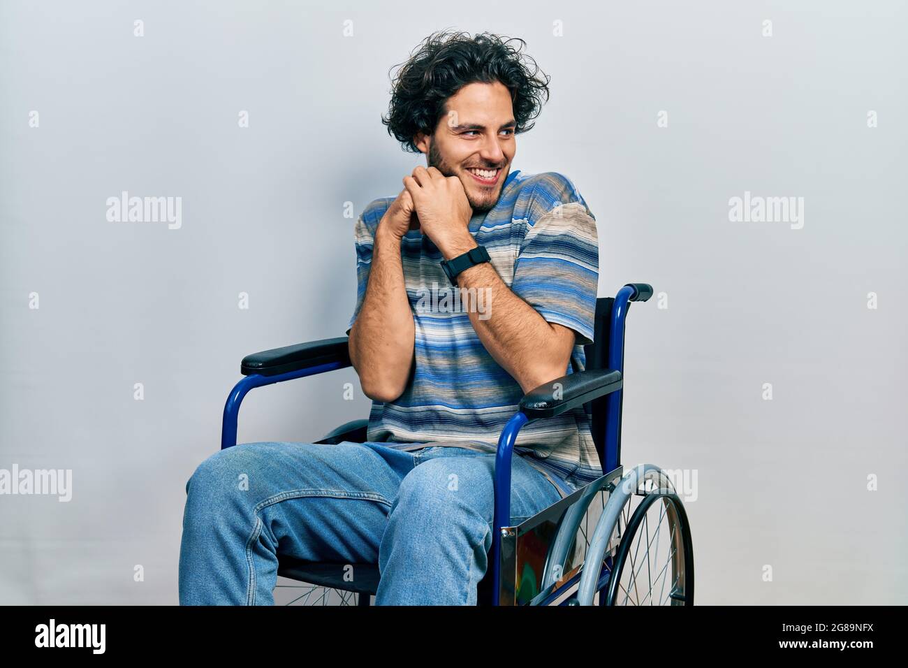 Handsome hispanic man sitting on wheelchair laughing nervous and ...
